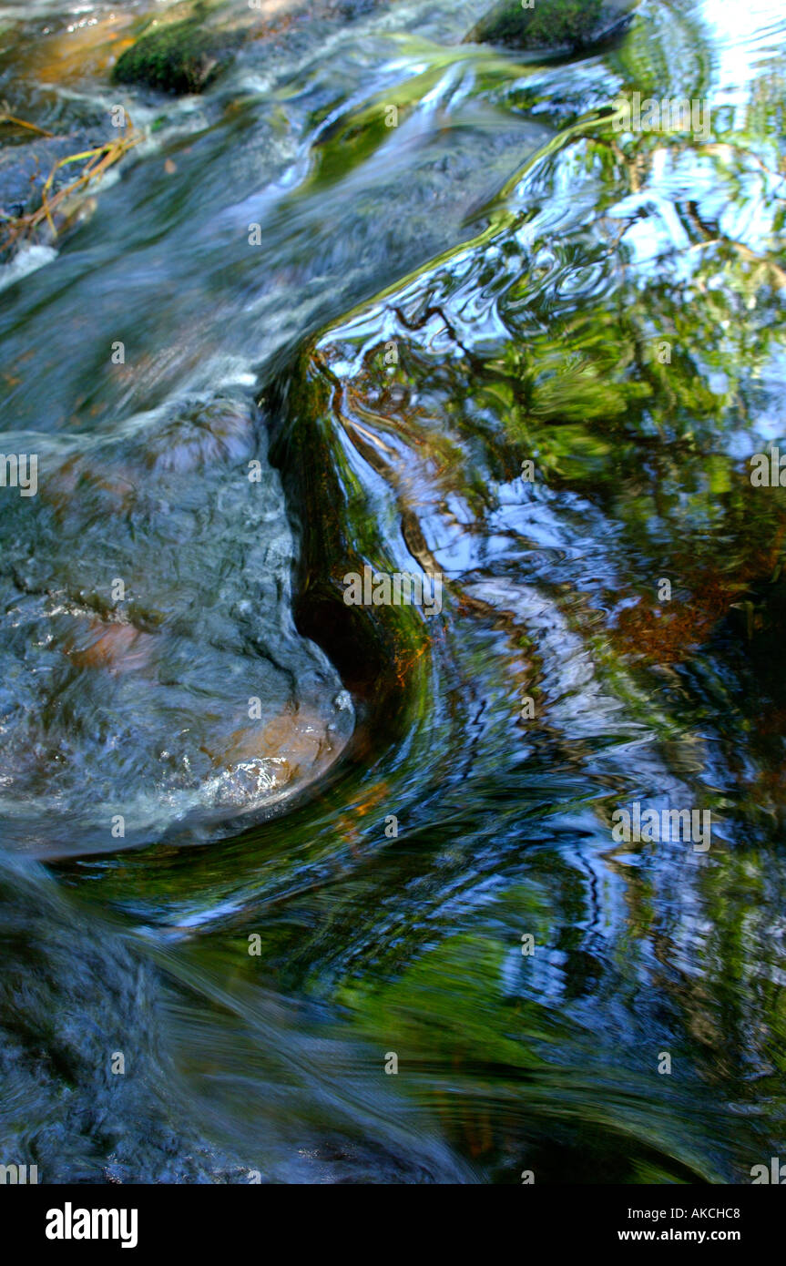 River flowing over submerged ridge of rock creating abstract shapes ...