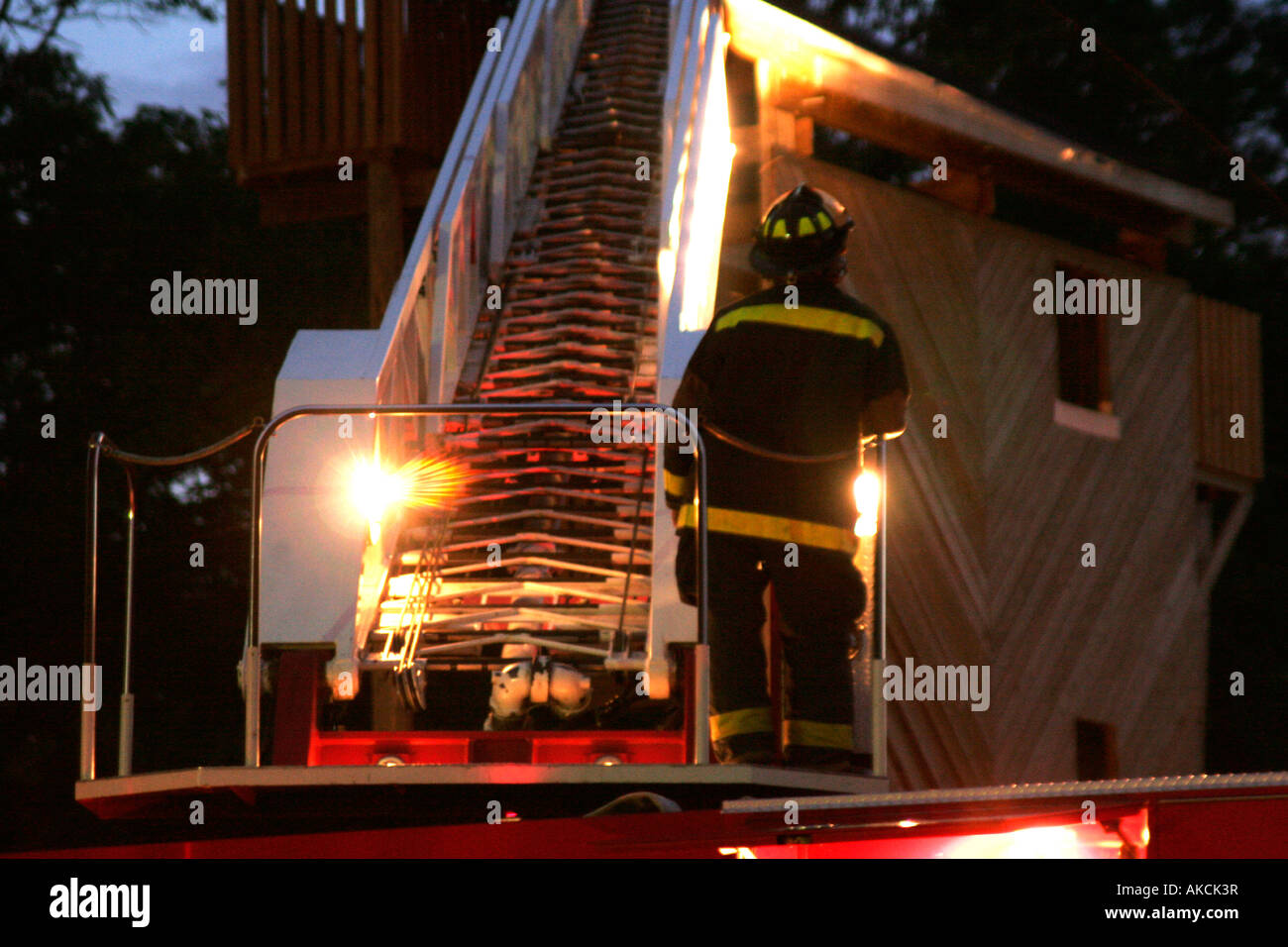 Firefighter standing at the controls of an extended ladder at a ...