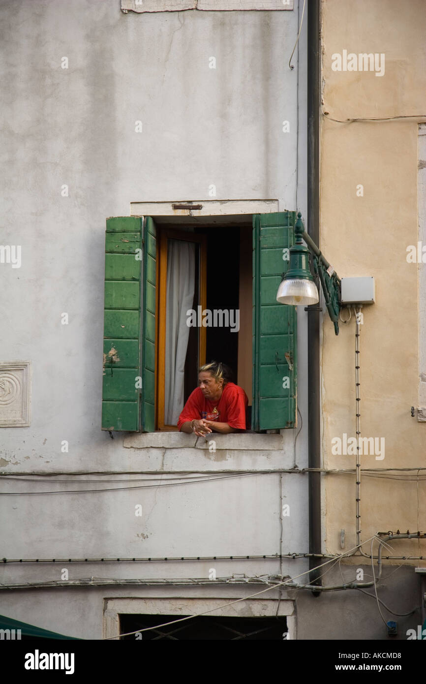 Italian woman leans on window sill watching neighborhood activity below ...