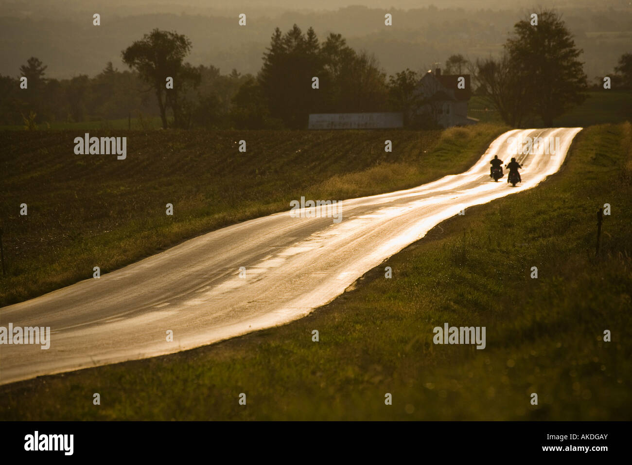 Two bikers motorcycles on a road in late afternoon sun upstate New York ...