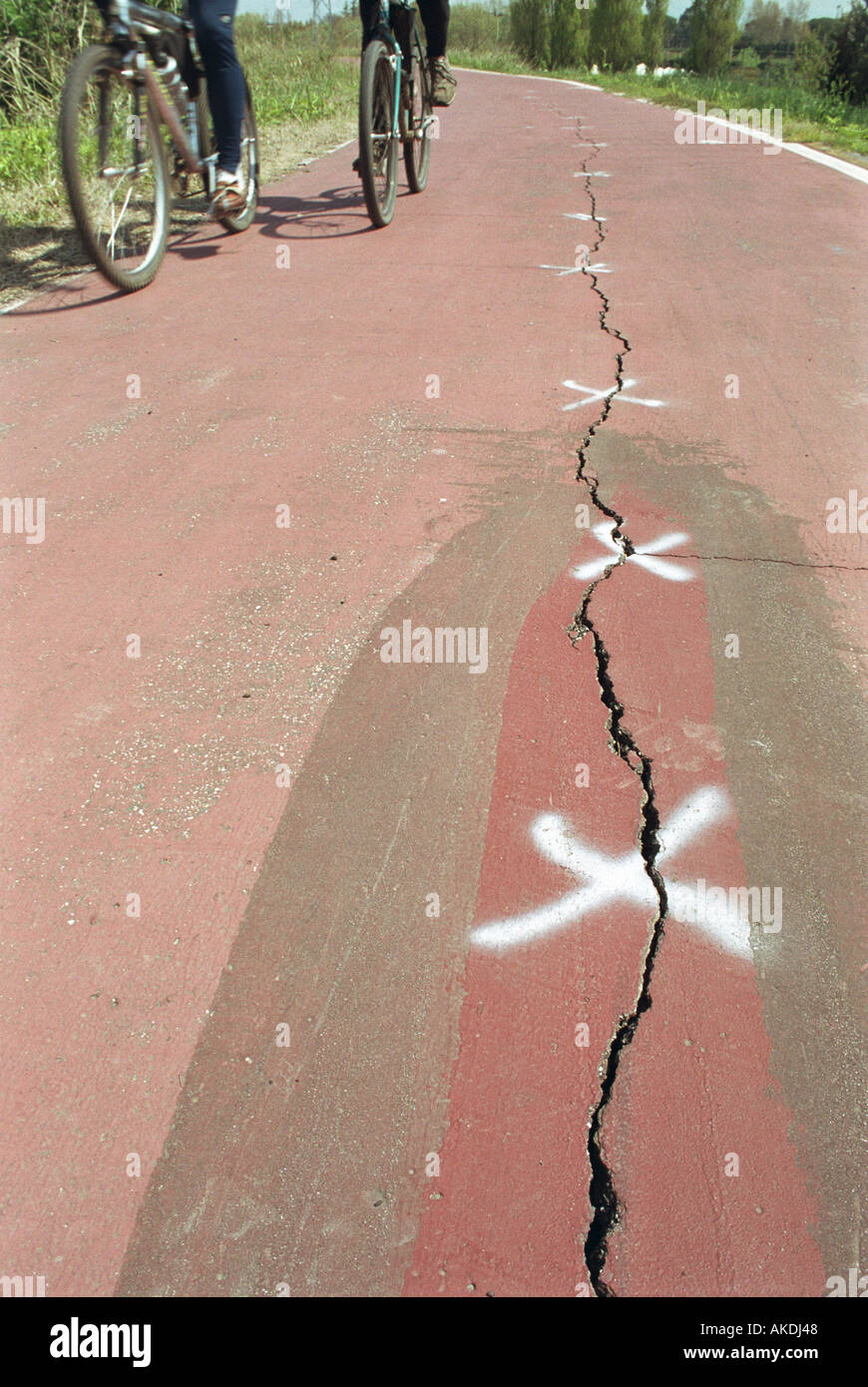 white paint crosses marking cracks in road surface with two cyclists ...