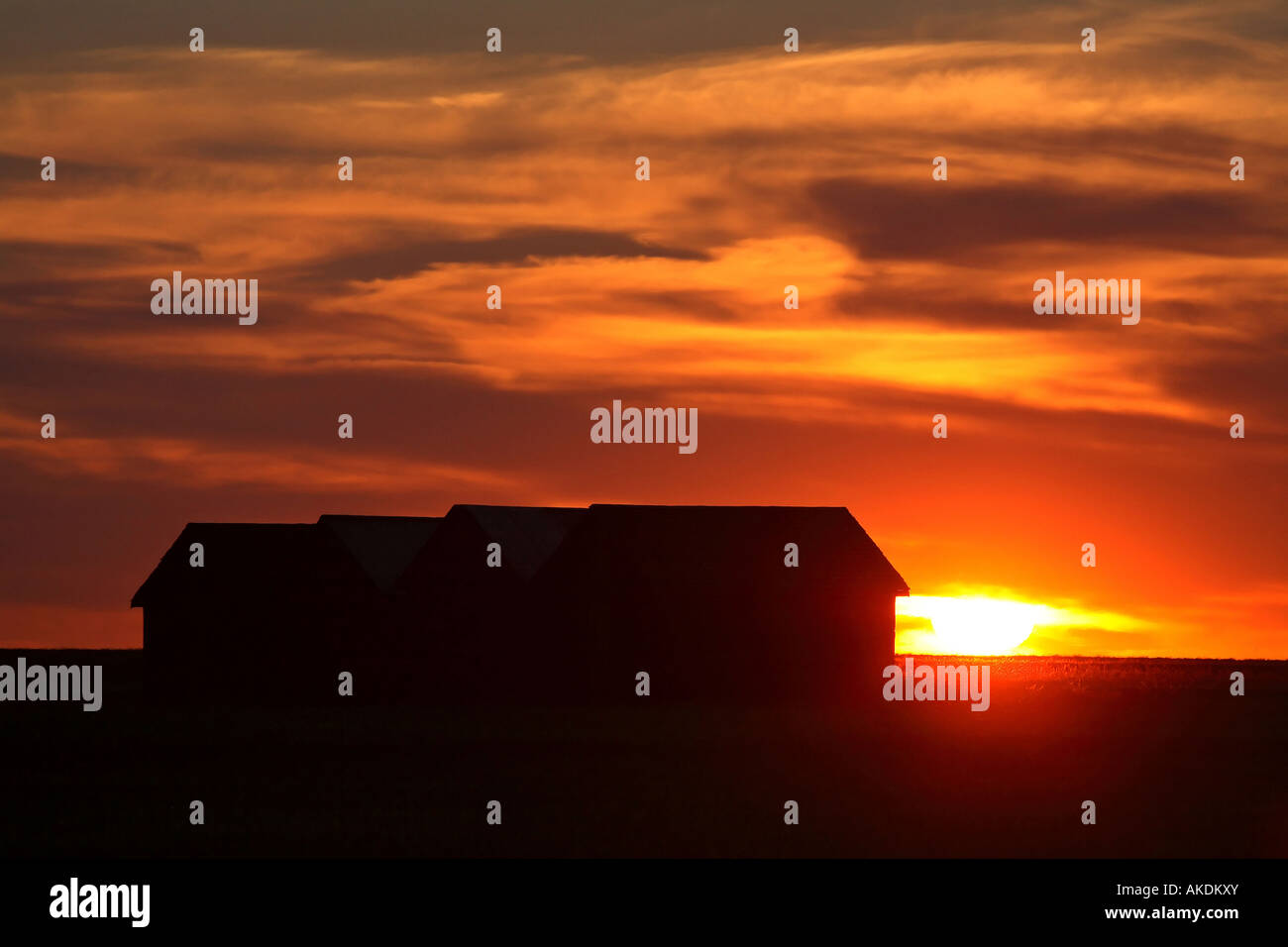 Sun setting behind old farm building Stock Photo - Alamy