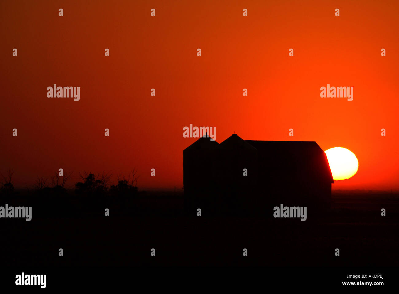 Sun setting behind farm building Stock Photo - Alamy