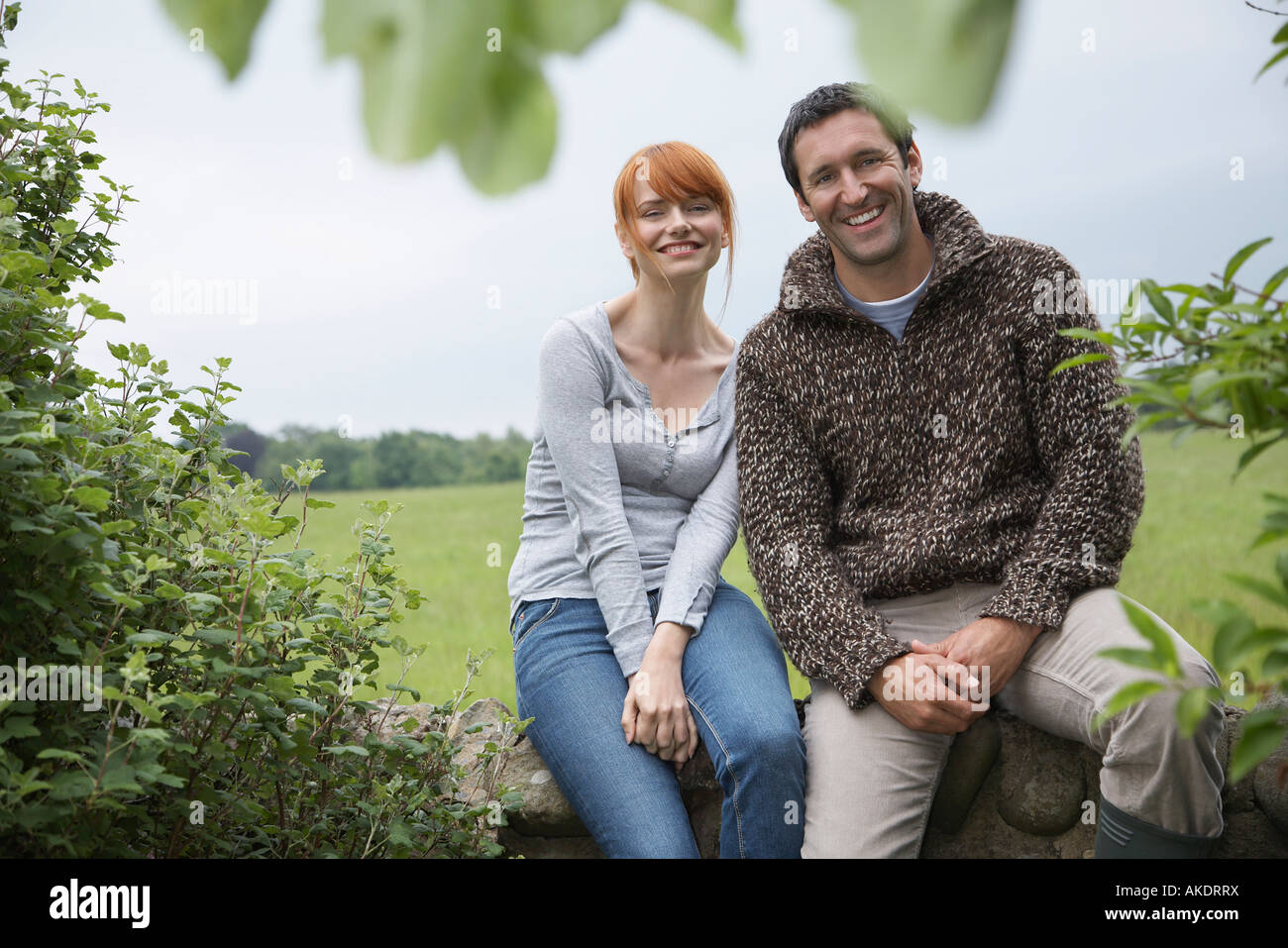 Couple sitting side by side on wall in countryside, portrait Stock ...