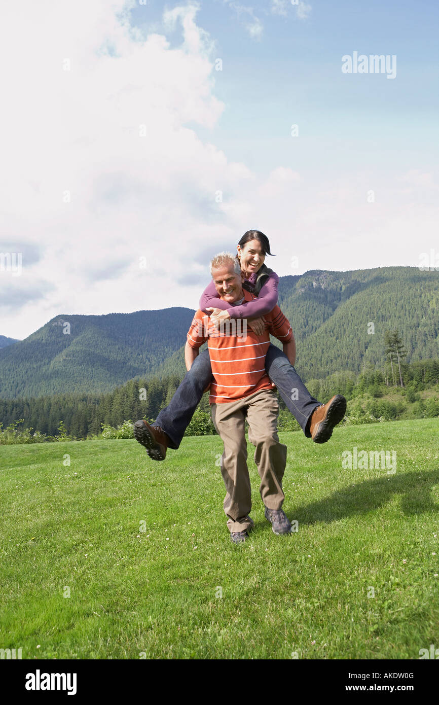 Man carrying woman piggy back in meadow, laughing Stock Photo - Alamy