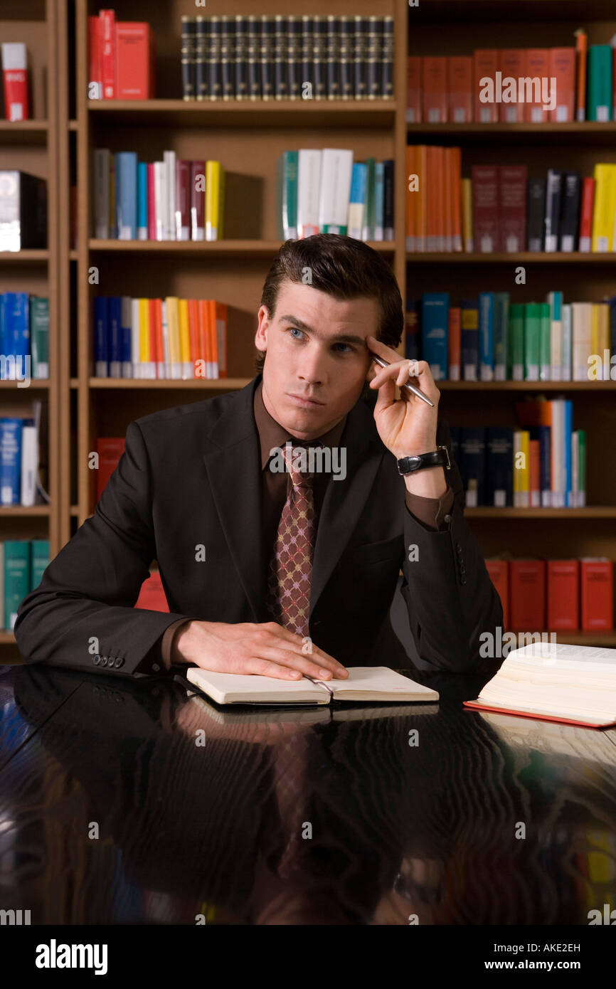 Pensive man wearing suit with book at desk in library Stock Photo - Alamy