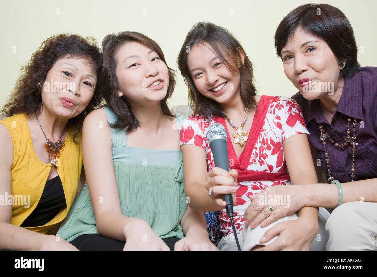Portrait of two young women singing with their grandmothers into ...