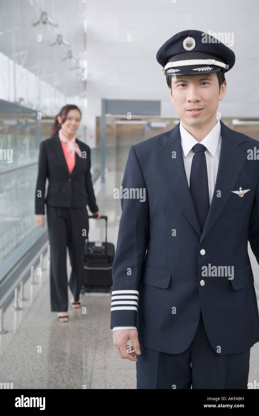Portrait of a male pilot with a female cabin crew walking behind him ...