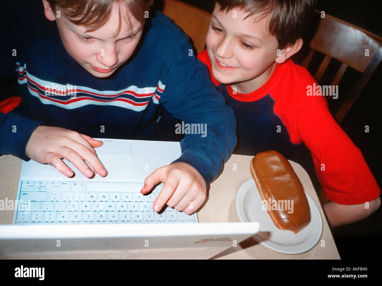 two boys playing a computer game on a laptop in a cafe one boy has a ...