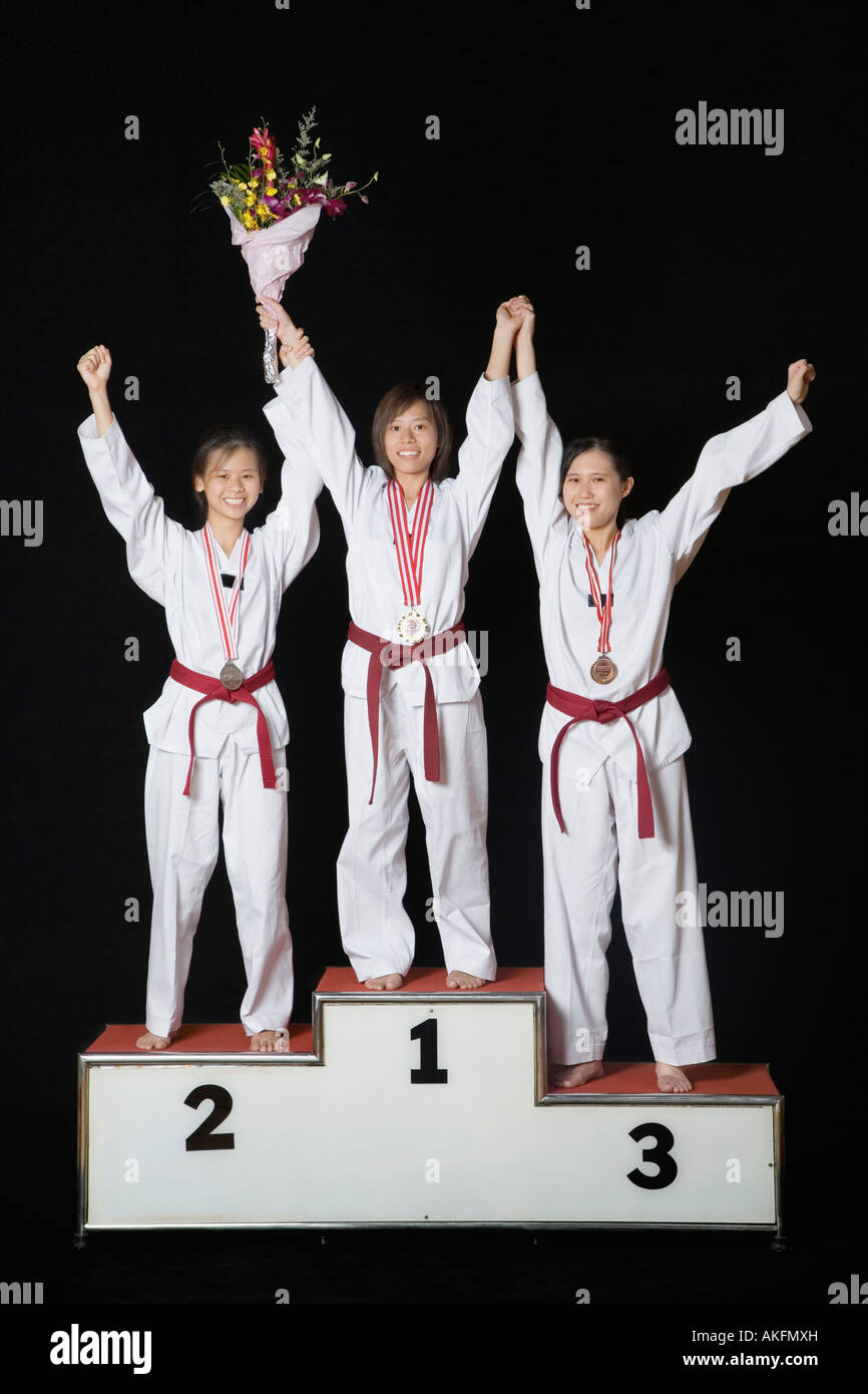 Three young women raising their hands on a winners podium Stock Photo ...