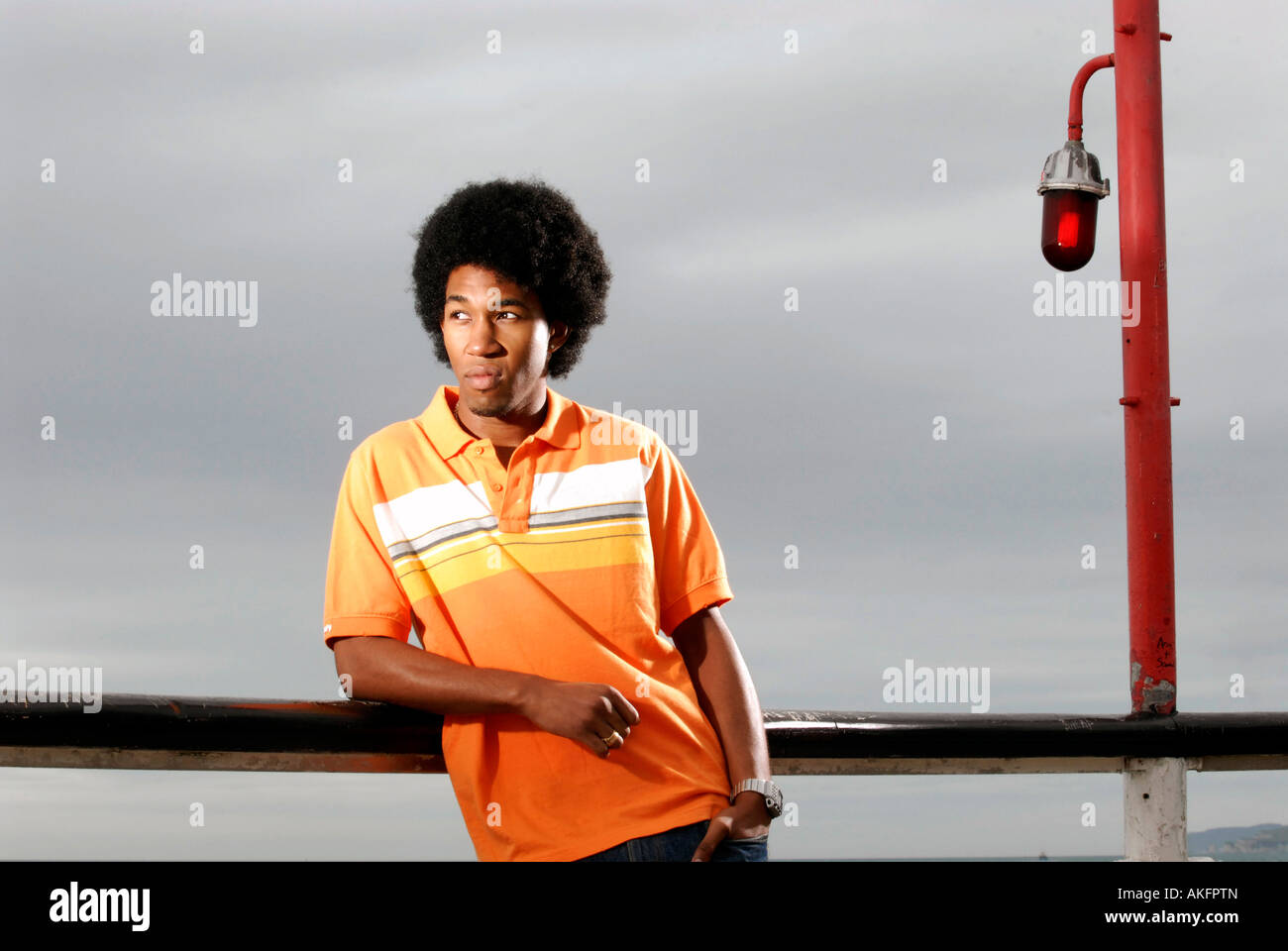 A young cool black man leaning against a rail at the end of Bournemouth ...