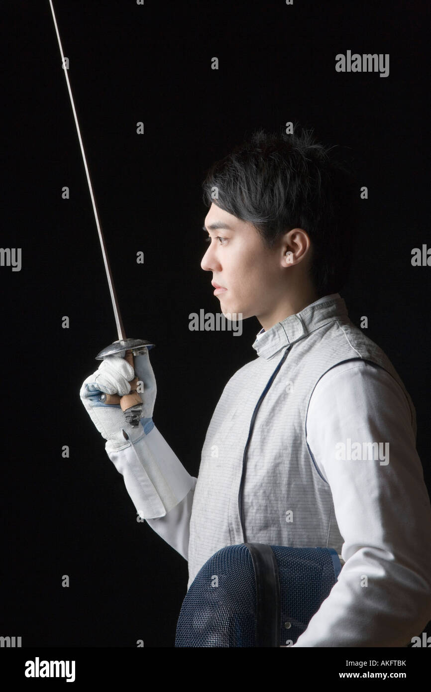 Side profile of a male fencer holding a fencing foil and a fencing mask ...