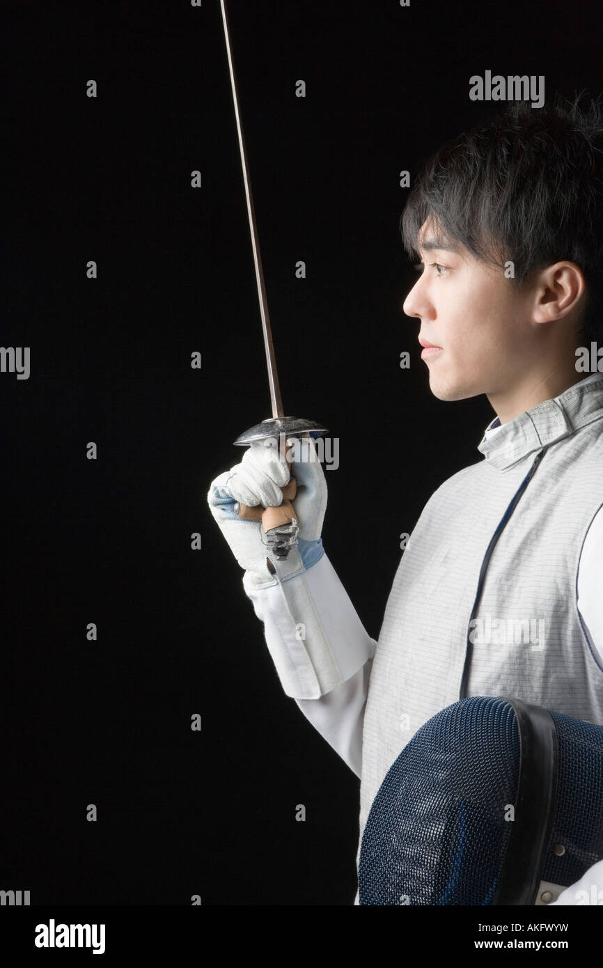 Side profile of a male fencer holding a fencing foil and a fencing mask ...