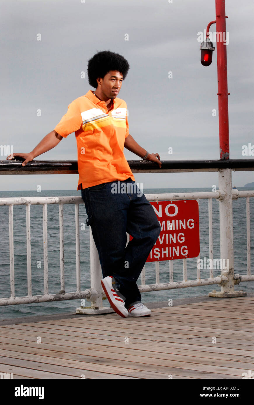 A young cool black man leaning against a rail at the end of Bournemouth ...