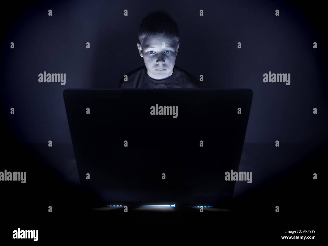 12 year old boy illuminated by the blue light of a computer monitor ...