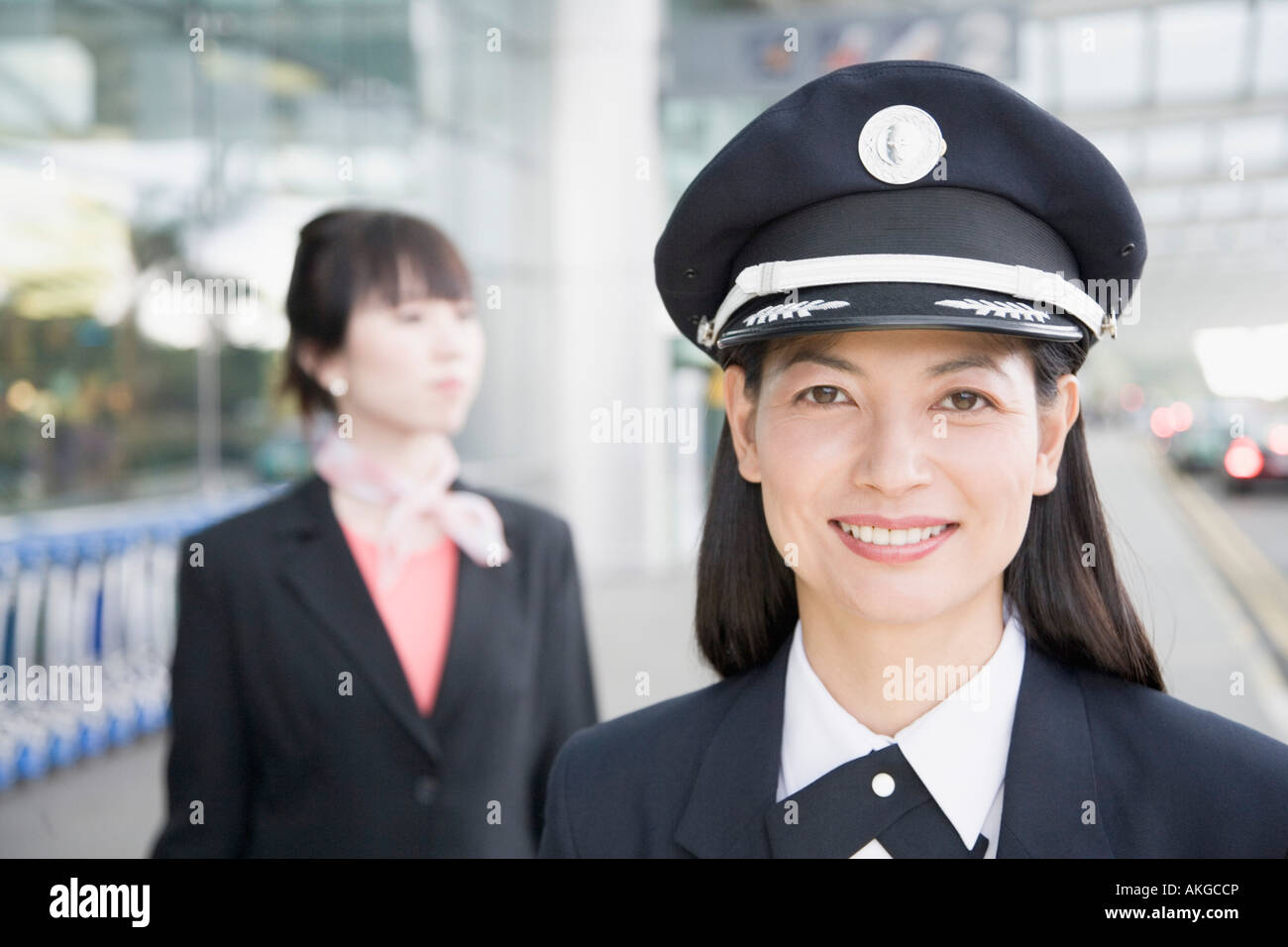 Close-up of a female pilot smiling with a female cabin crew behind her ...