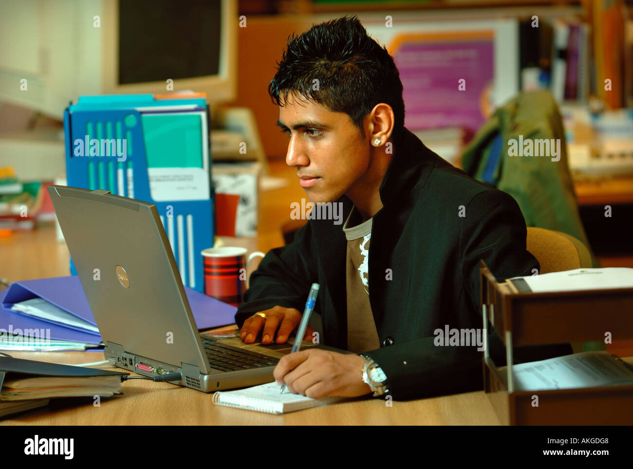 A TEENAGE BOY WORKING ON A LAPTOP COMPUTER IN AN OFFICE ENVIRONMENT UK ...