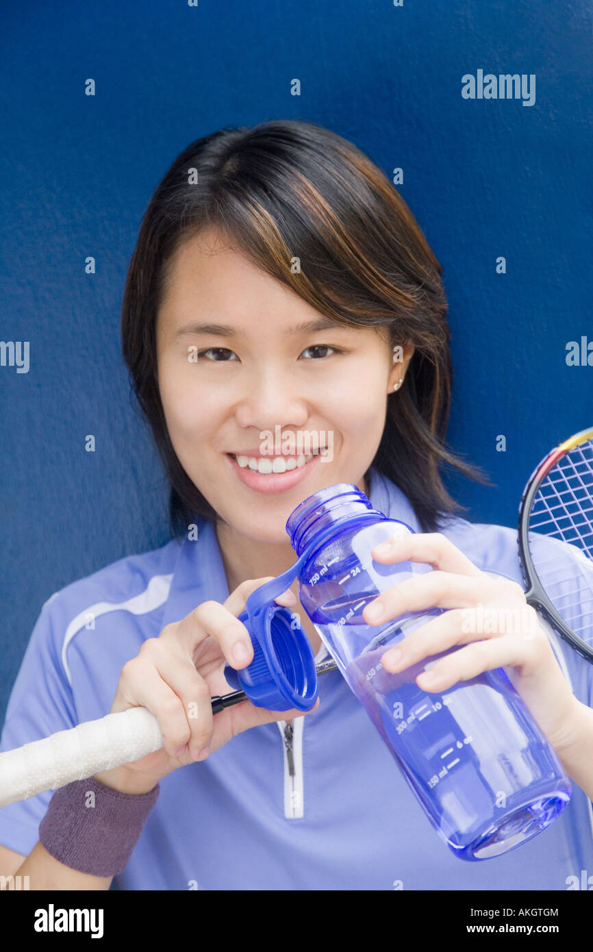 Portrait of a young woman holding a badminton racket and a water bottle ...