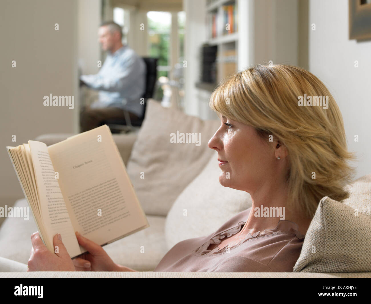 Woman reading a book on sofa Stock Photo - Alamy