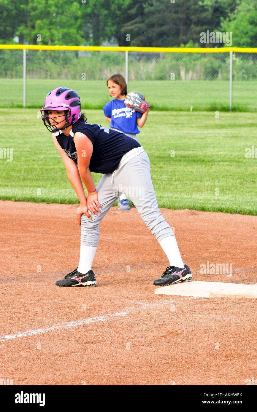 Female softball player waiting to run to third base wearing a pink and ...