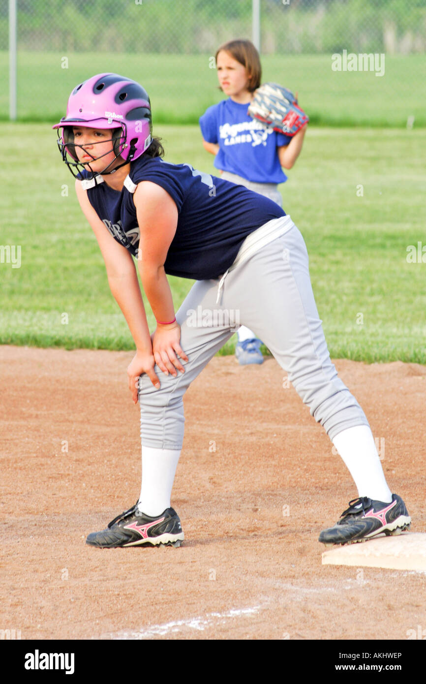 Female softball player waiting to run to third base wearing a pink and ...