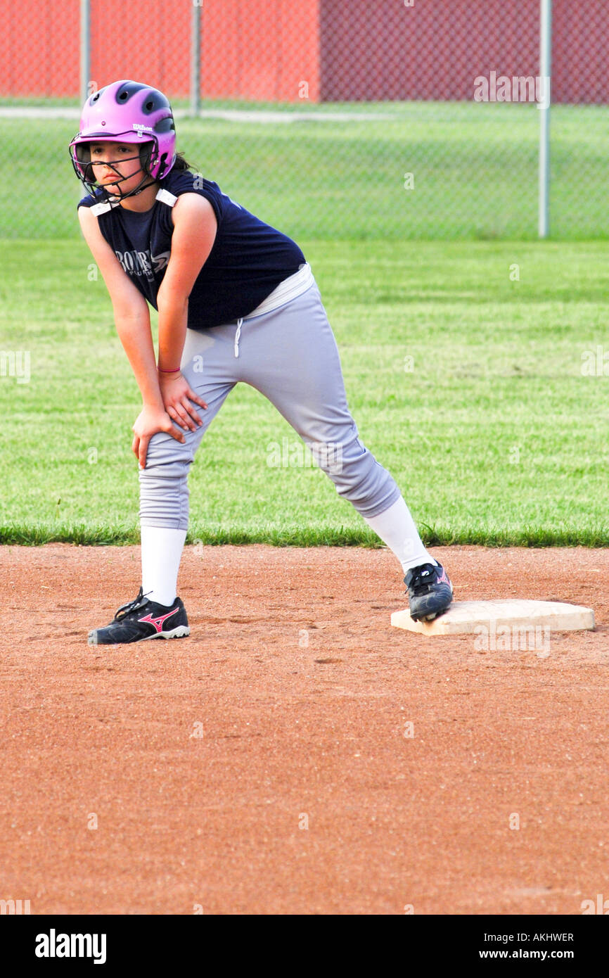 Female softball player waiting to run to third base wearing a pink and ...