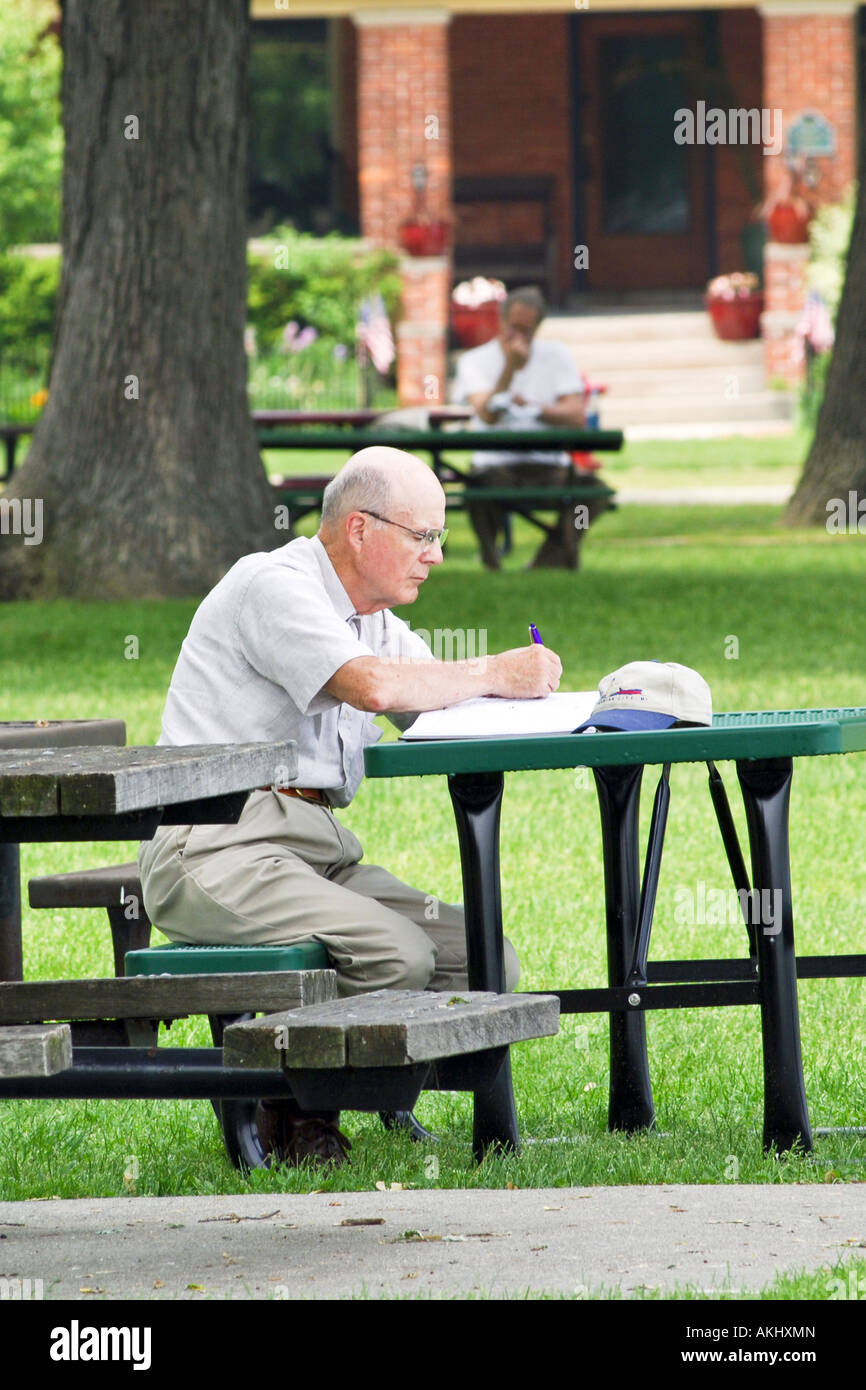 Male retiree sitting on at a park bench reading his book Stock Photo ...
