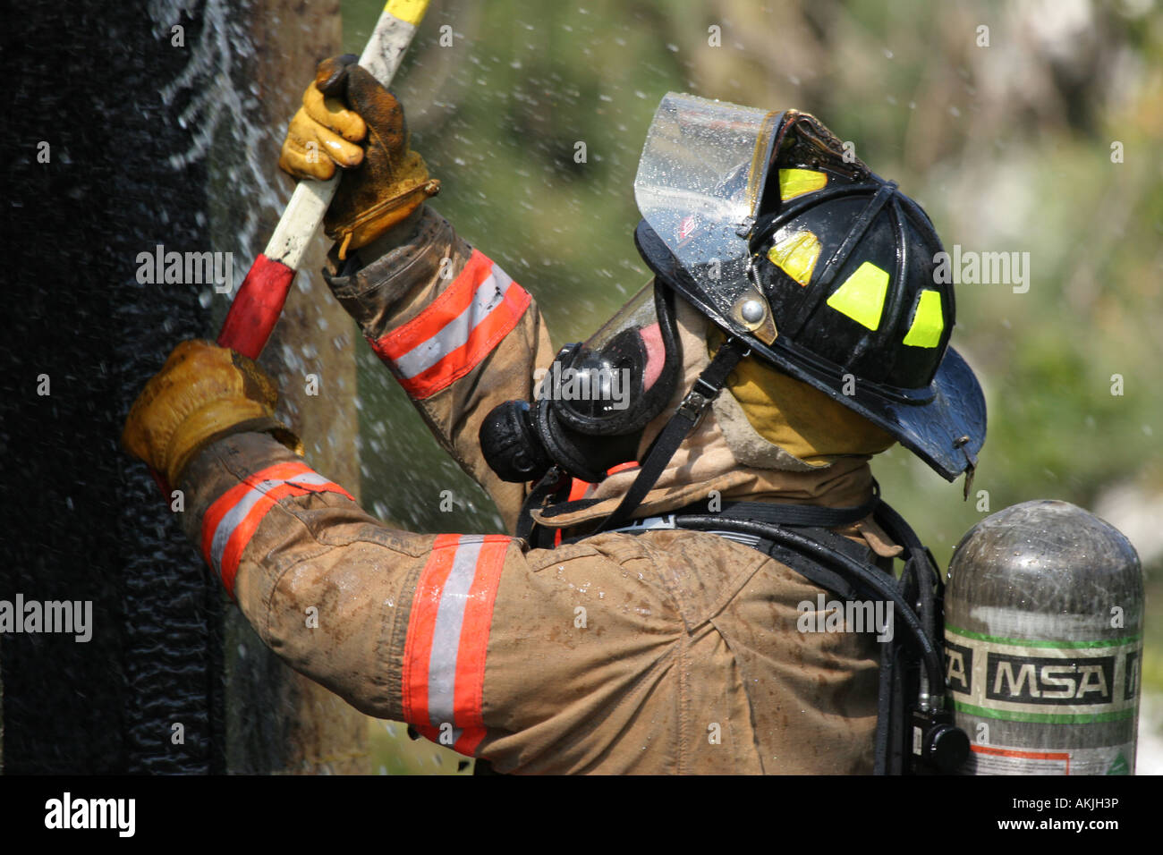 A firefighter using an ax on a structure fire with water being sprayed ...