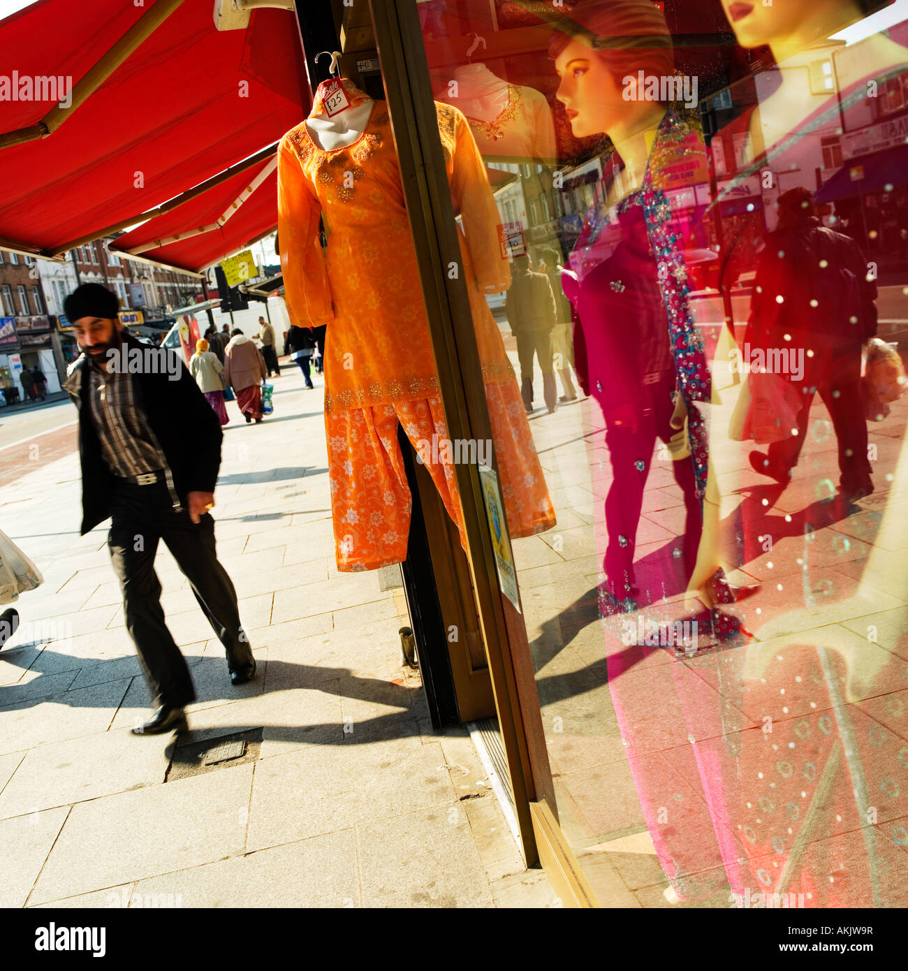 Sikh young man walking past reflections in sari shop window high street ...