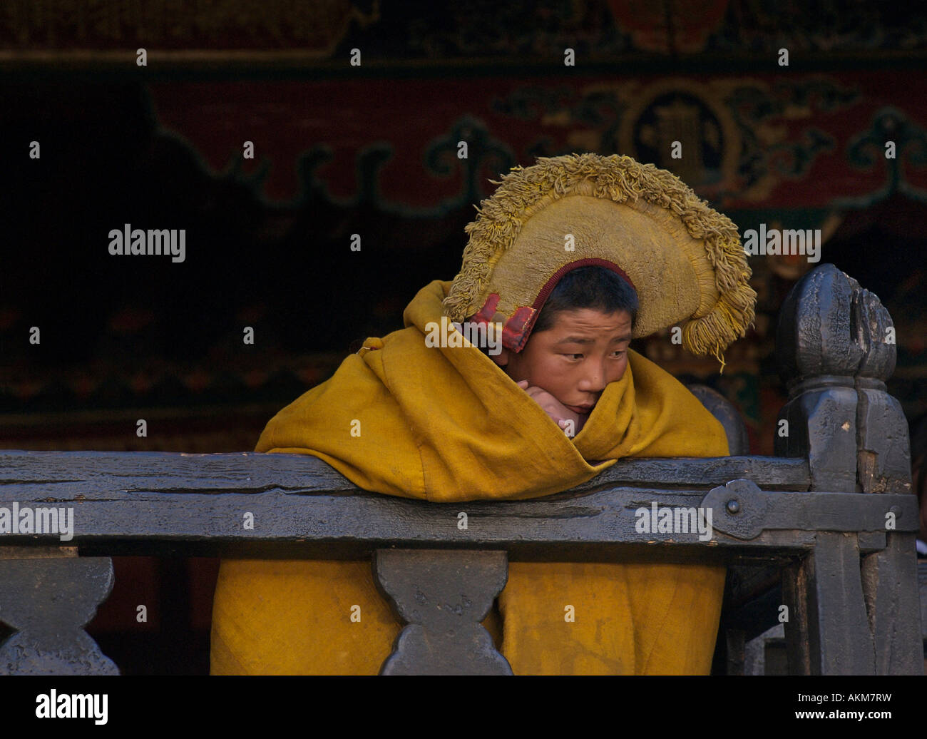 Novice monk in yellow robe and headwear peering over a balcony at ...