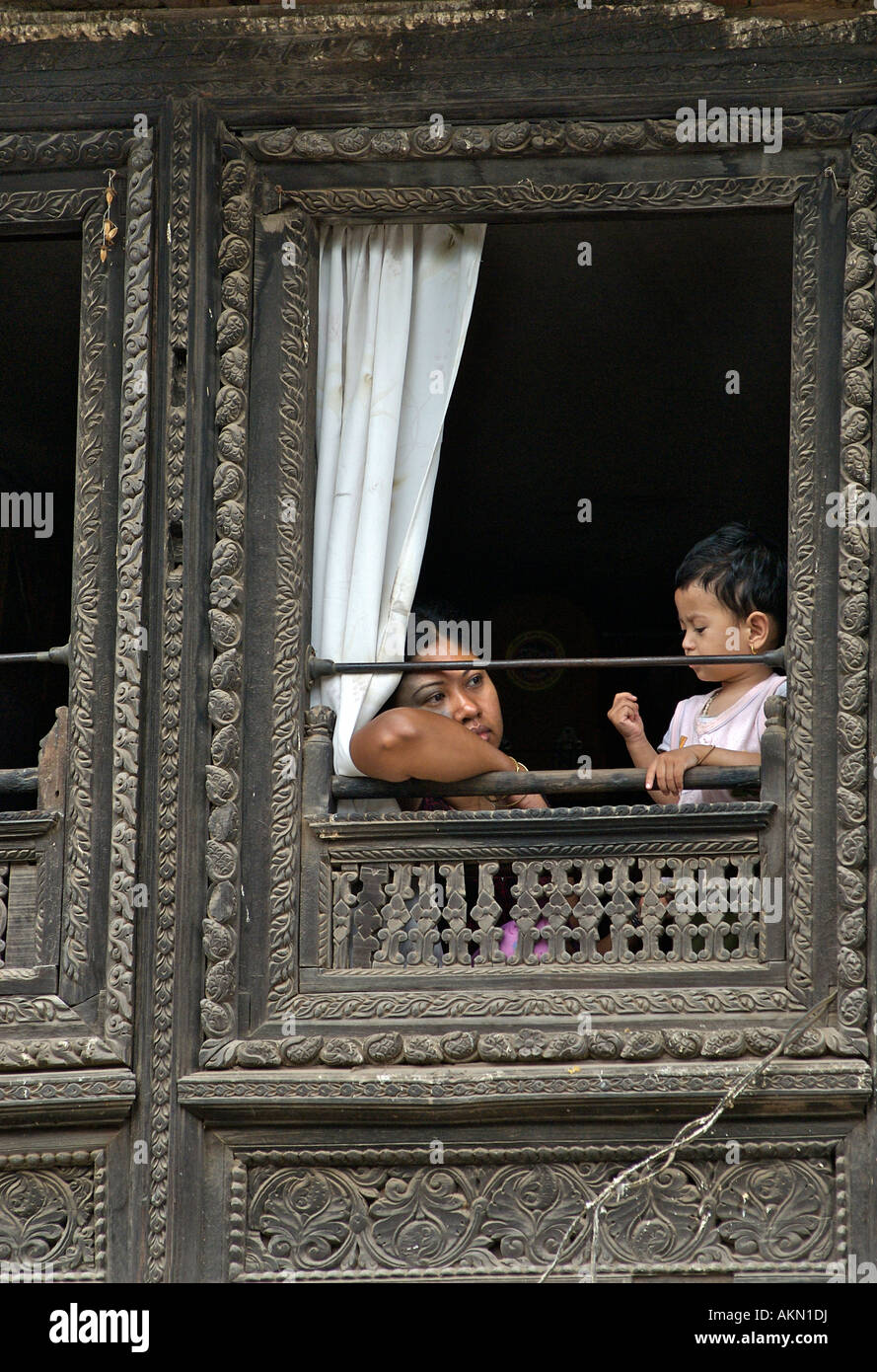 Mother and child looking out of an ornately carved window in the Patan ...