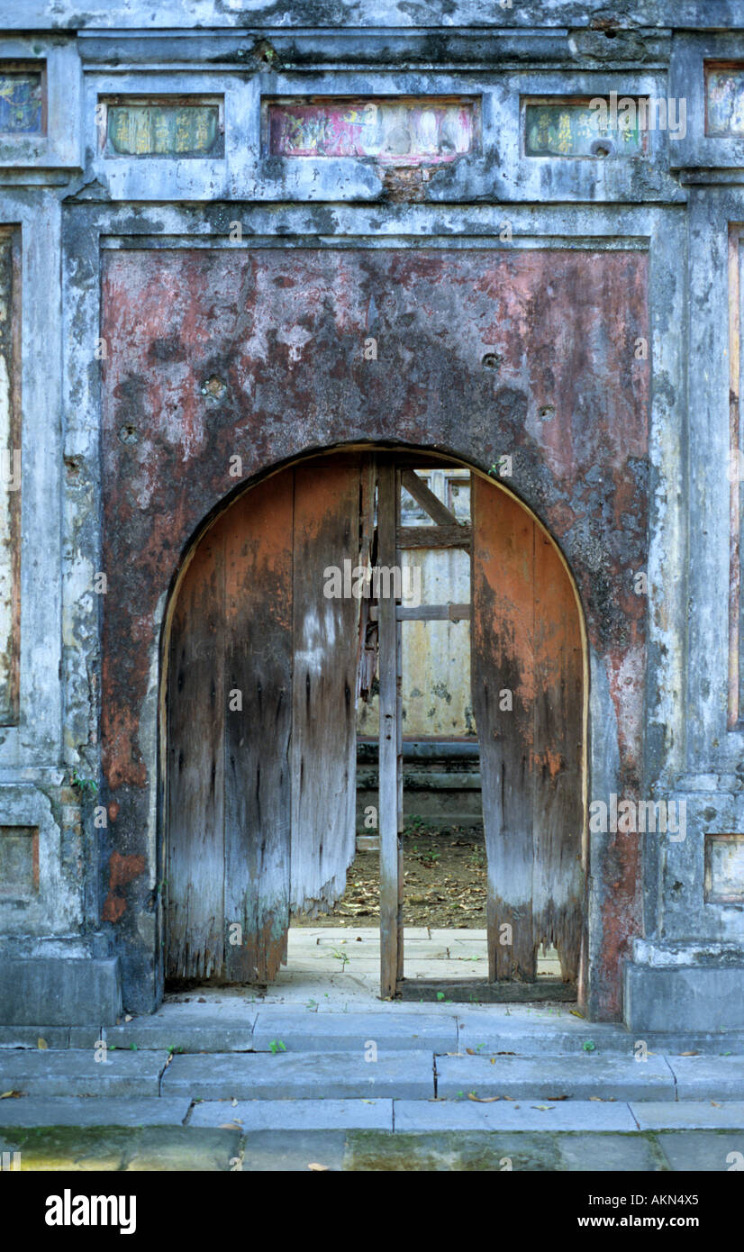 Arched opening in weathered decaying wall with broken wooden doors ...