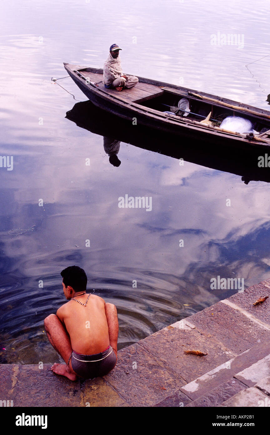 One Indian male crouching at the edge of the Ganges River on Ghat steps ...