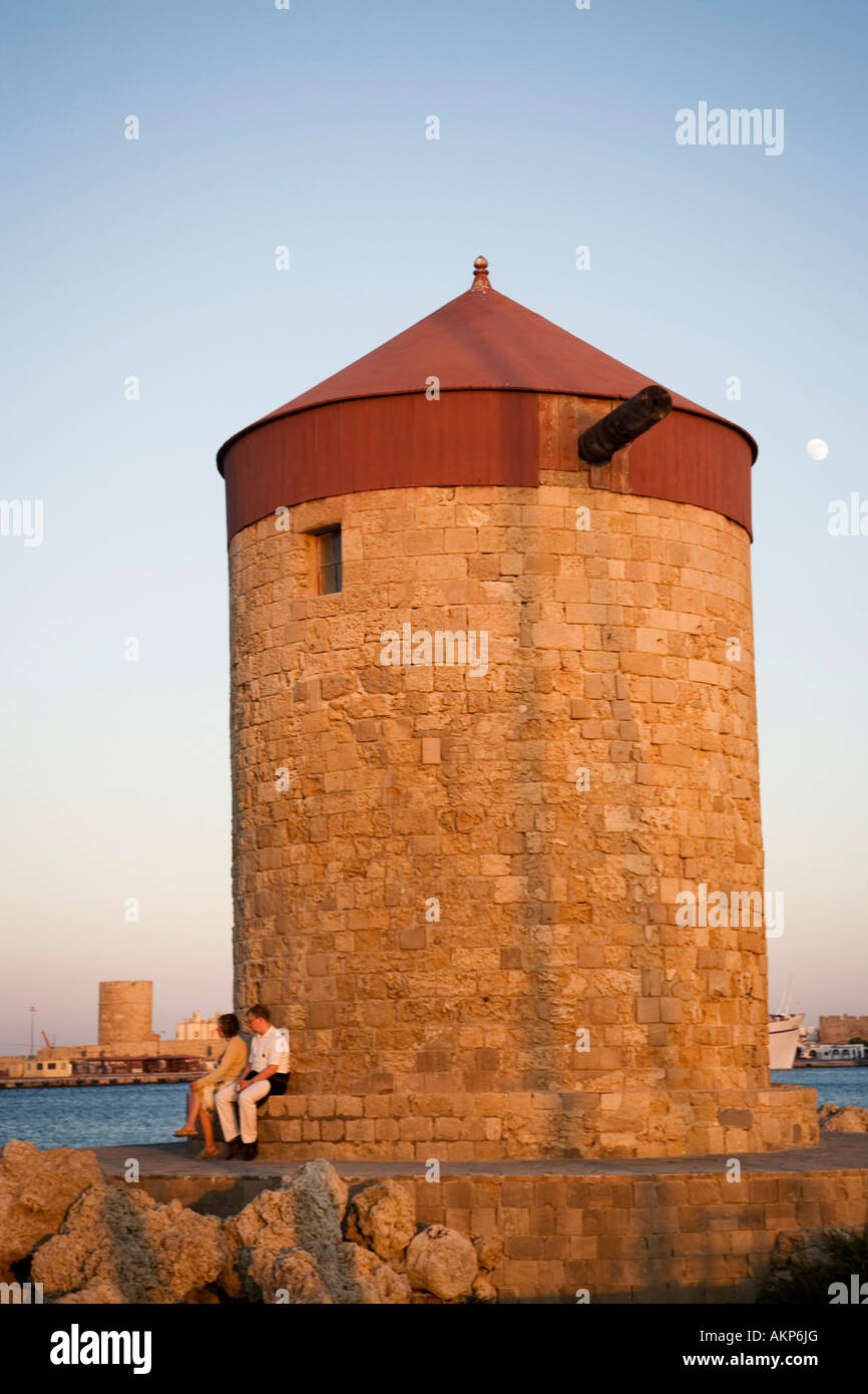 Couple sitting windmill on mole at Mandraki harbour translated ...