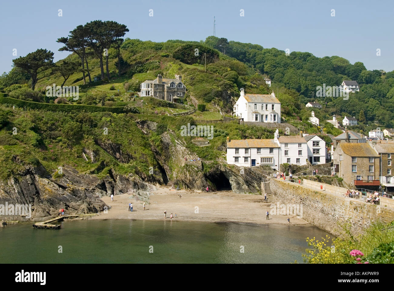 Tourists walking English village harbour wall beside coastal beach ...