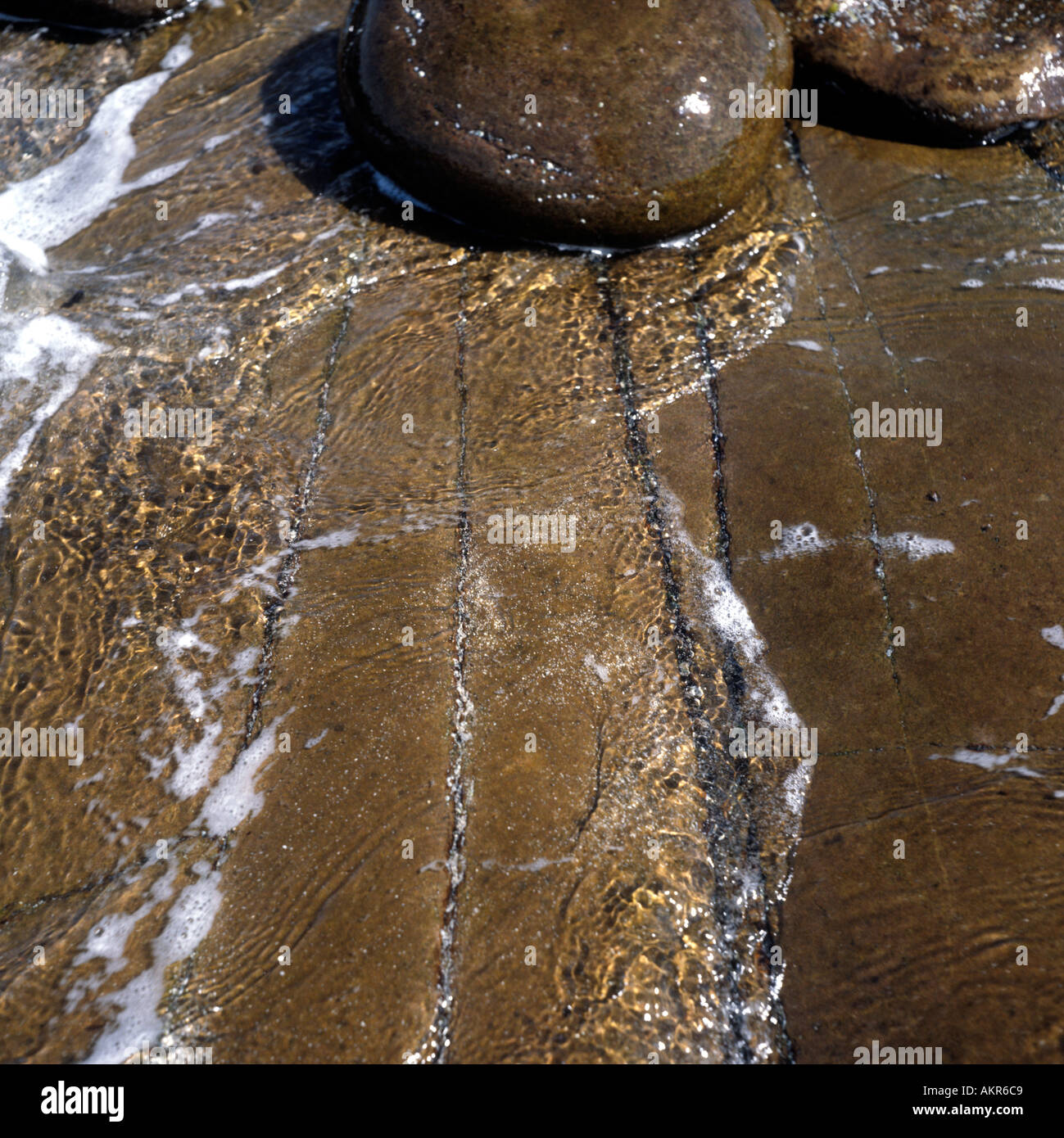 Wave water lapping against large brown round pebble on smooth brown ...