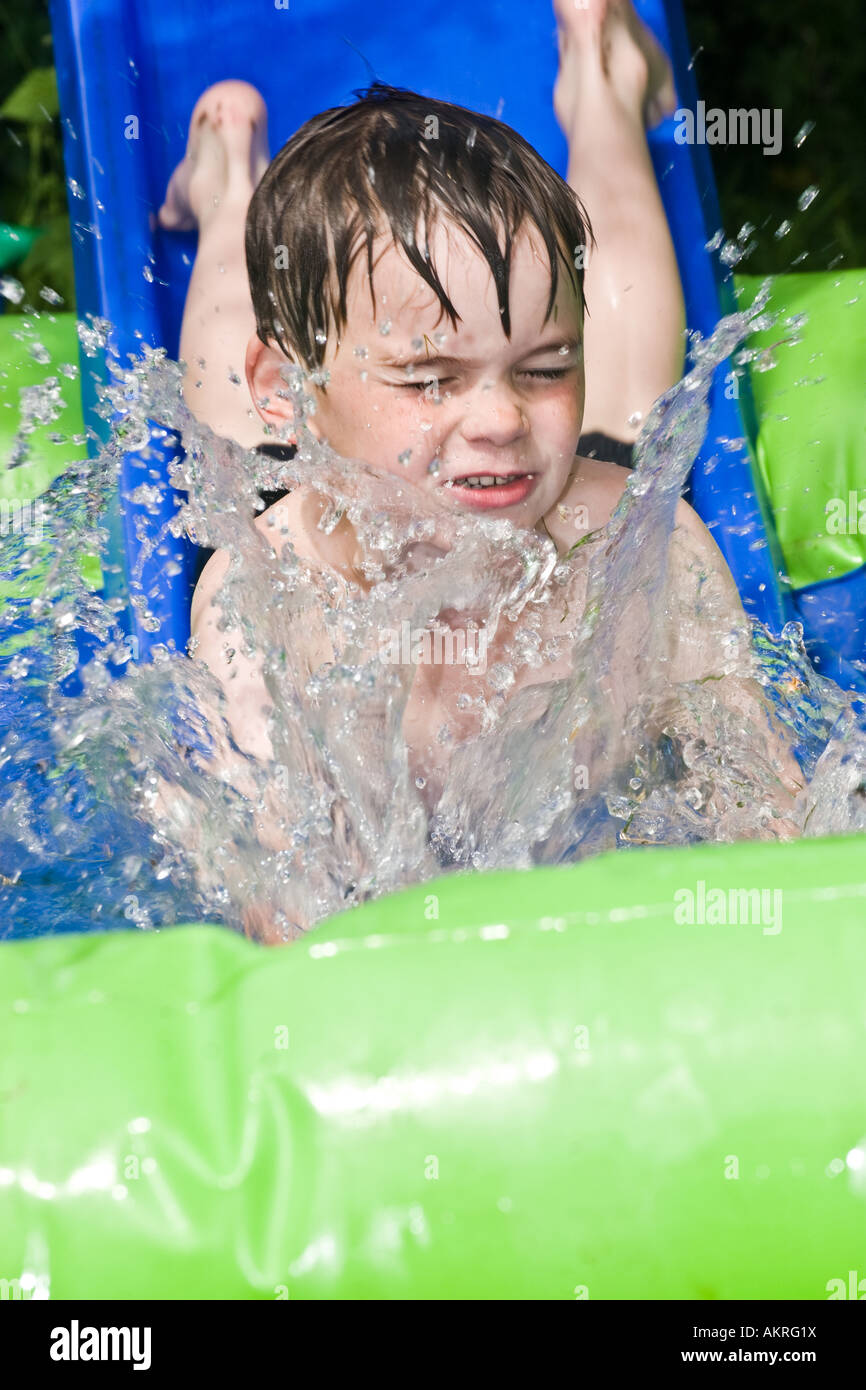 Children Sliding Forwards Down A Slide Into A Paddling Pool Full Of Water In A Surrey Garden 