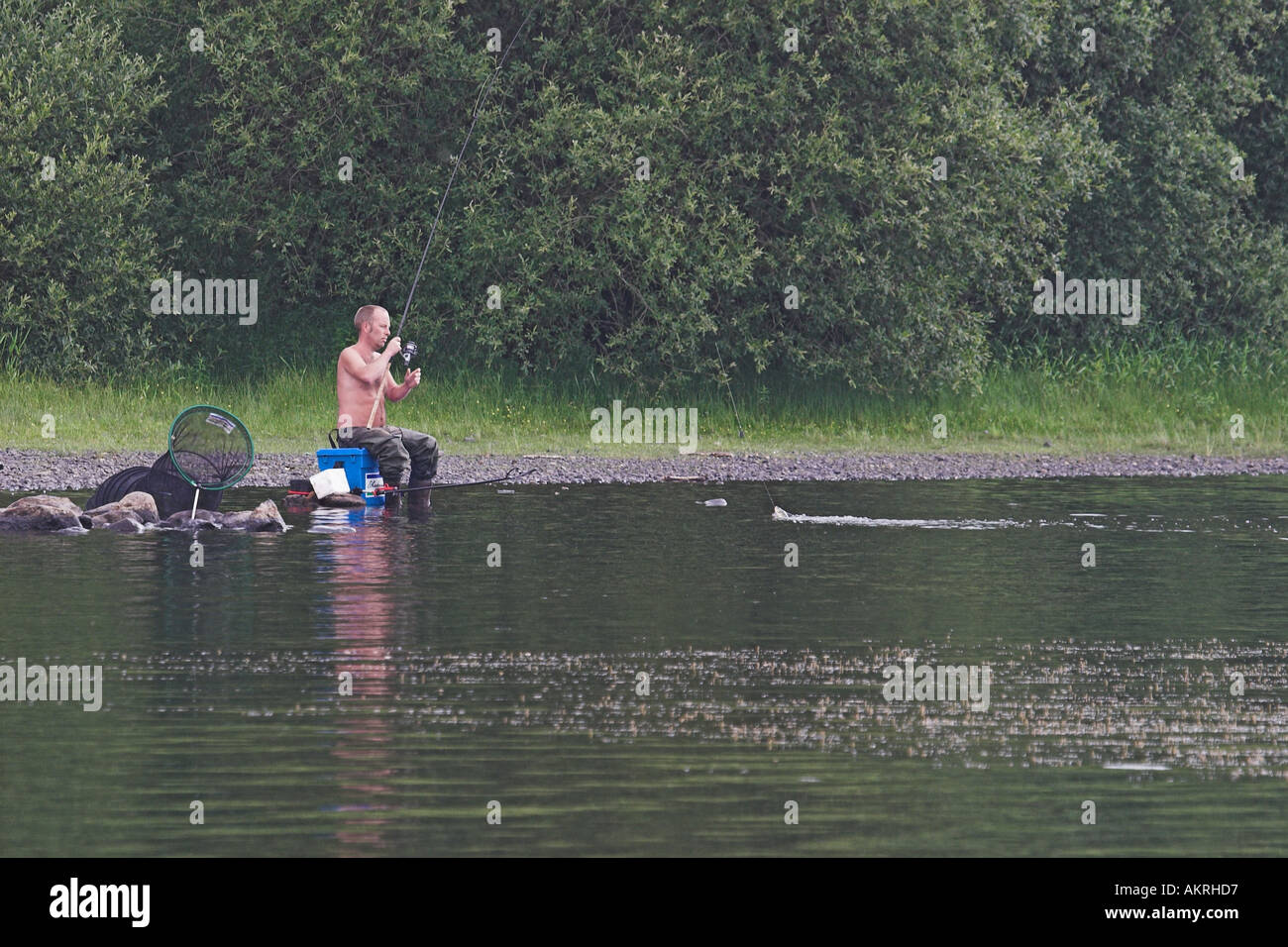 fisherman on a lakes edge fishing with net and rod Stock Photo - Alamy