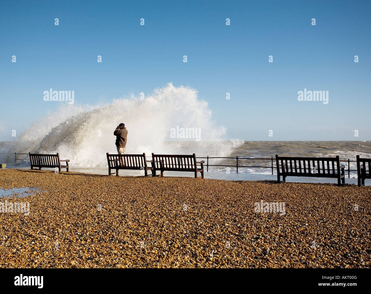 man standing on seafront bench observing large wave smashing against ...