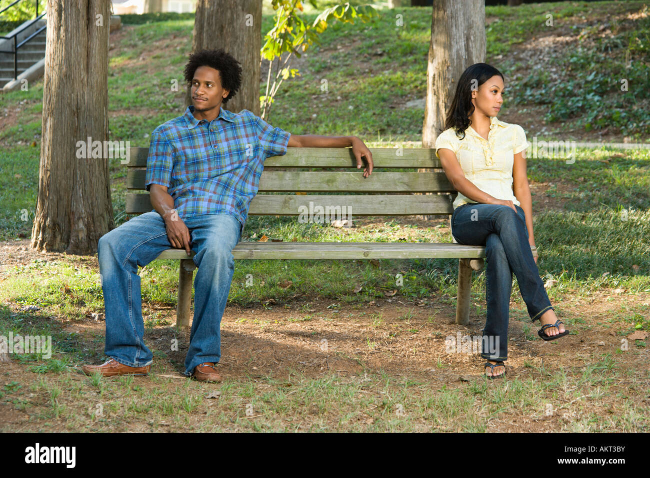 Man and woman sitting on opposite sides of park bench looking away from ...
