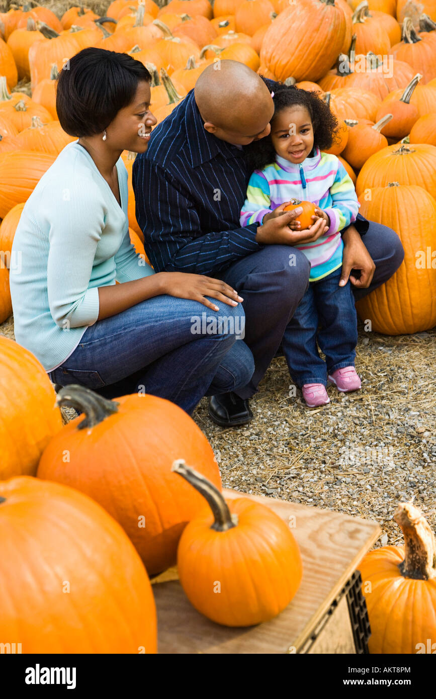 Parents and daughter picking out pumpkin and smiling at outdoor market ...
