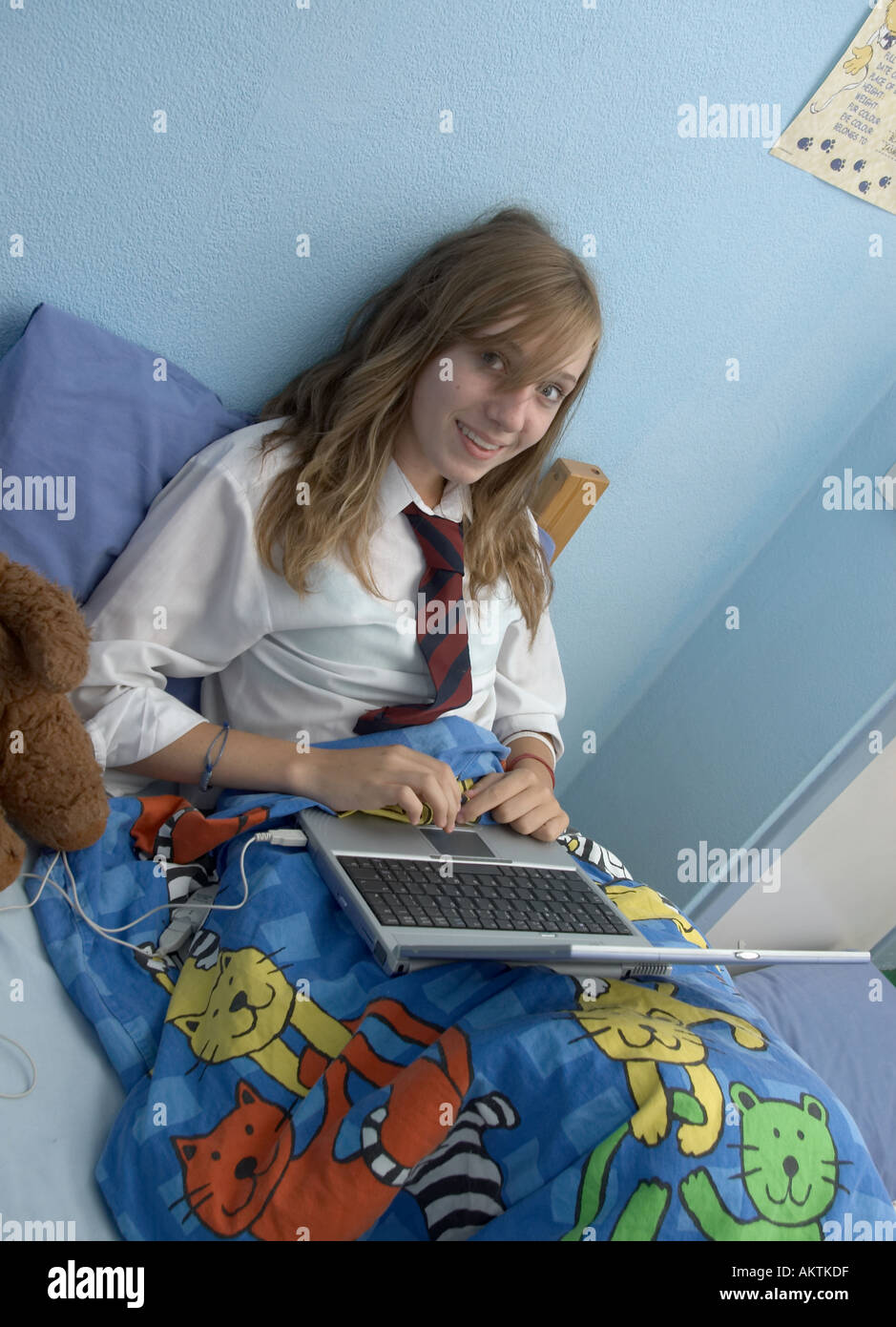 a smiling schoolgirl doing homework in her bed on a laptop computer ...