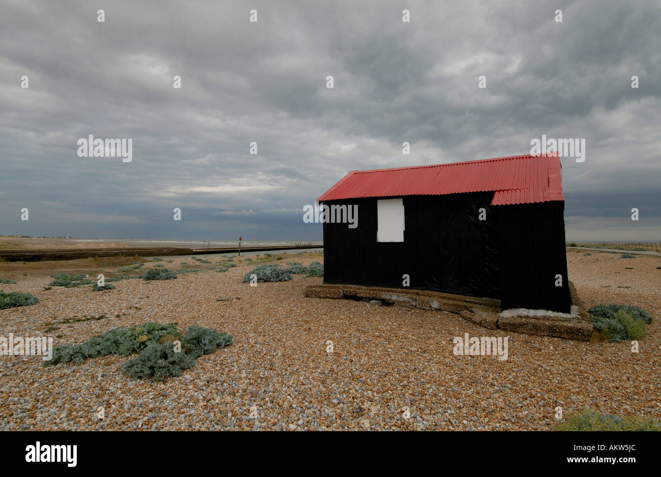 Red roofed and black corrugated iron hut on the shingle above the mouth ...