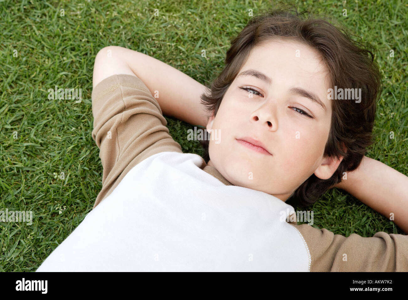 Pre-teen boy lying on back in grass, hands behind head, elevated view ...