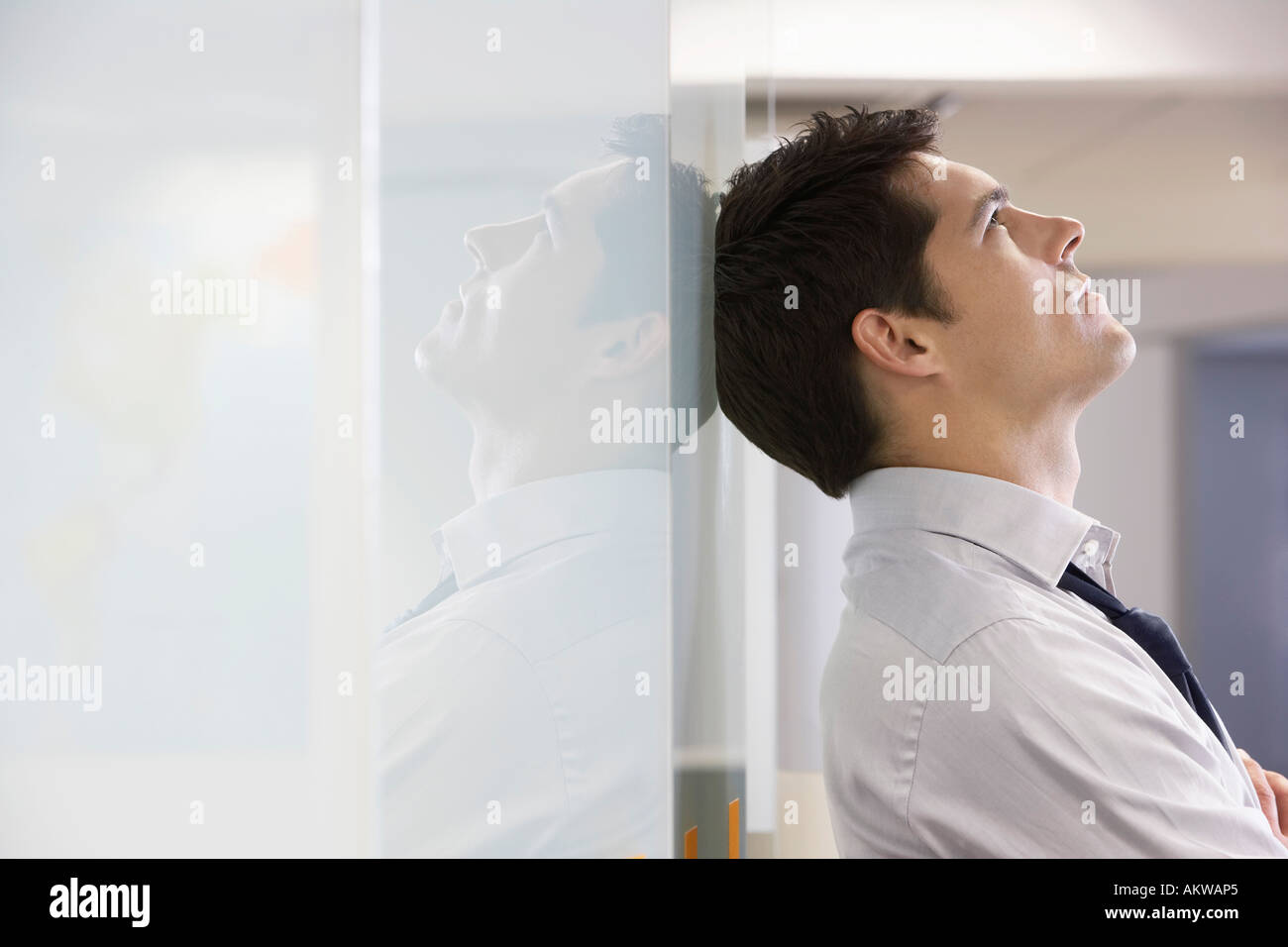 Unhappy Businessman leaning back against office wall and looking at ...