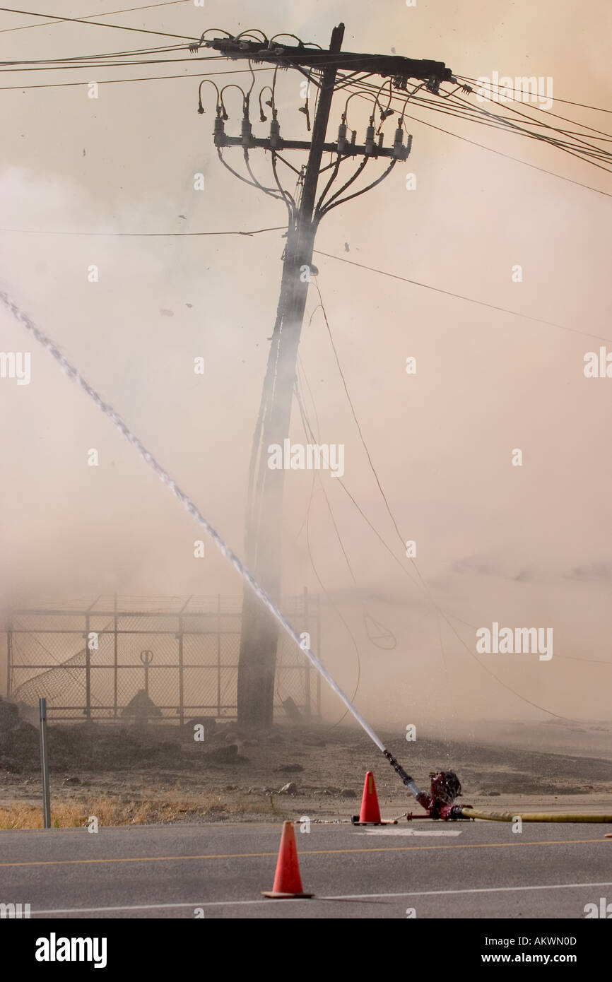 Water being sprayed on a large industrial fire with a burned power pole ...