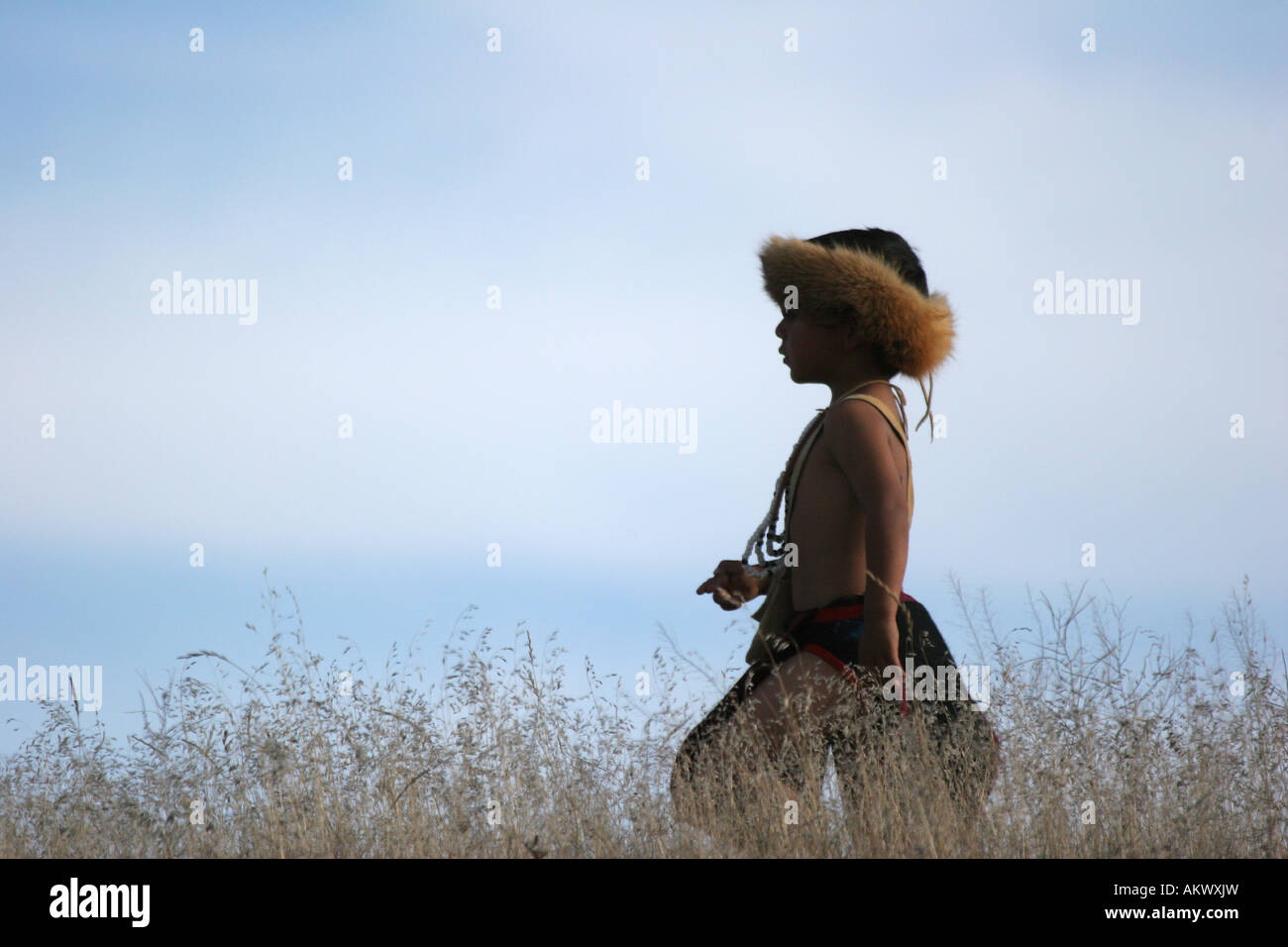 A Native American Indian boy running in the dried grasses with a fur ...