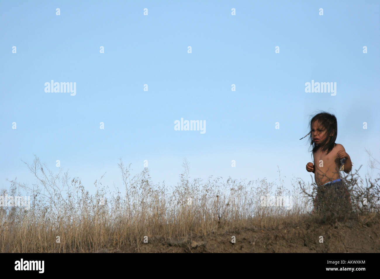 A Native American Indian boy running in the dried grasses looking upset ...