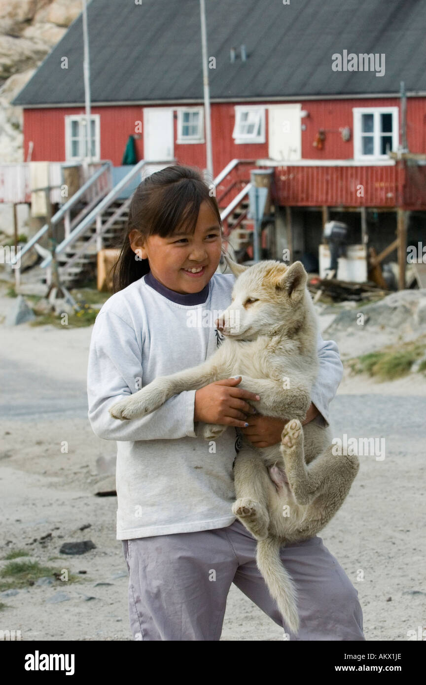 Young Inuk girl with a greenland dog puppy with typical houses in ...