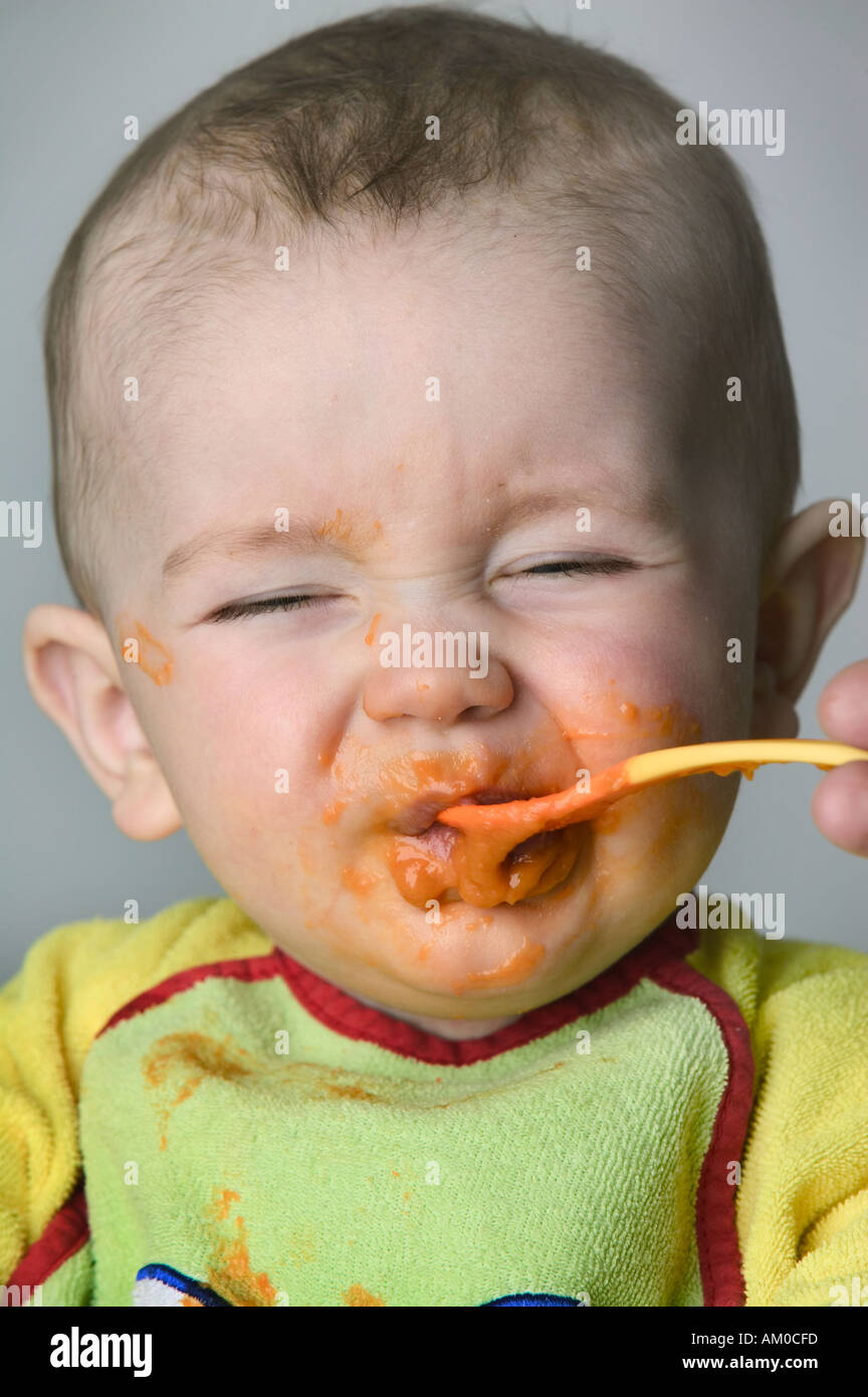 fed up looking baby of 8 months being spoon fed covered in food eyes ...